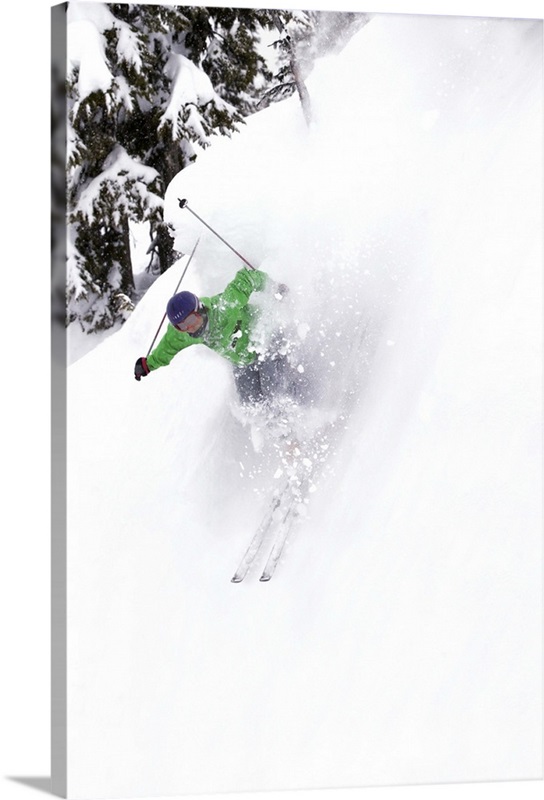 A free skier skis down a steep hill near trees, kicking up snow ...
