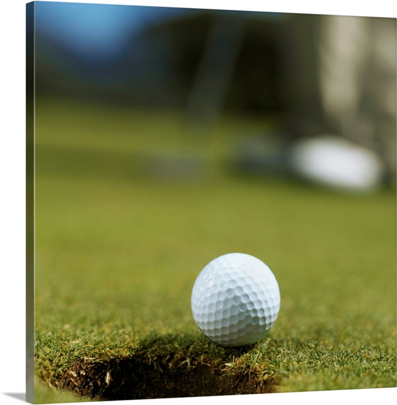 Golf ball about to fall into the hole with a golfer in the background ...