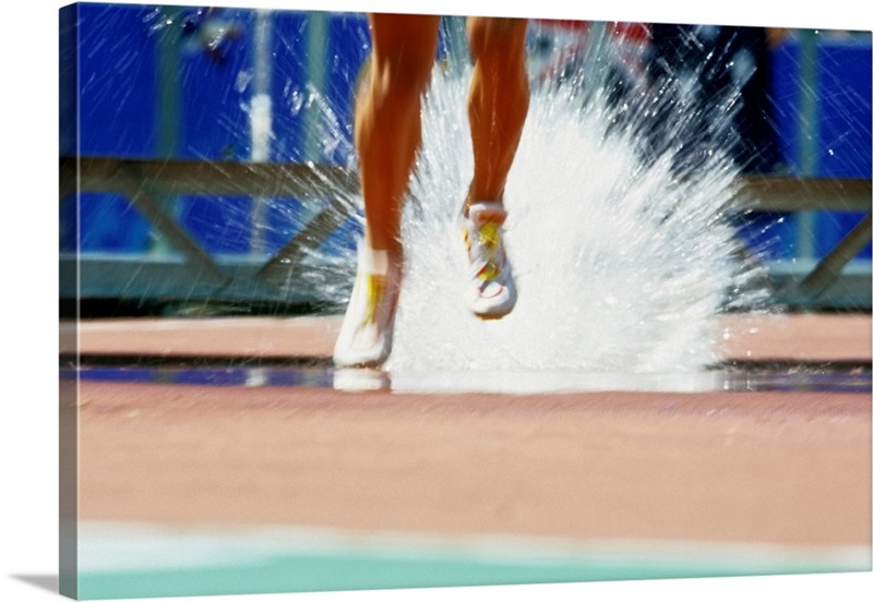 Runners' legs splashing through the water jump of a track and field ...