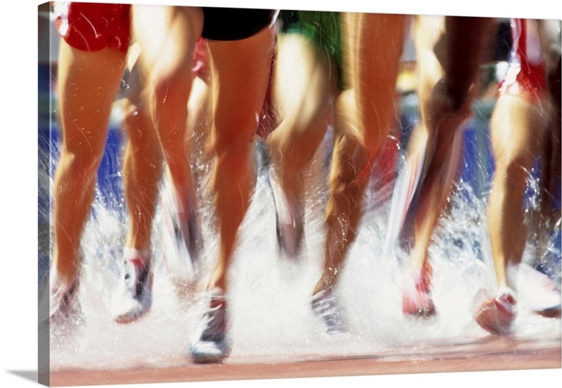 Runners' legs splashing through the water jump of a track and field ...