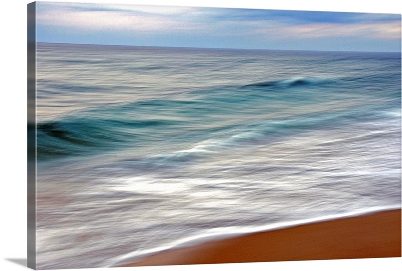Teal and white surf flows on a rust-colored beach under blue clouds ...